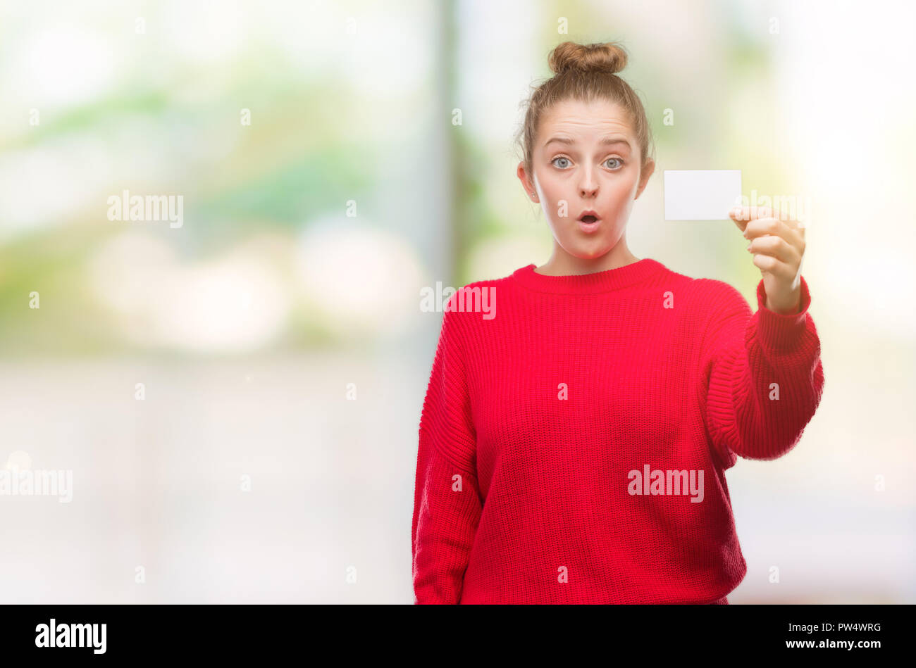 Young blonde woman holding advertising card scared in shock with a ...