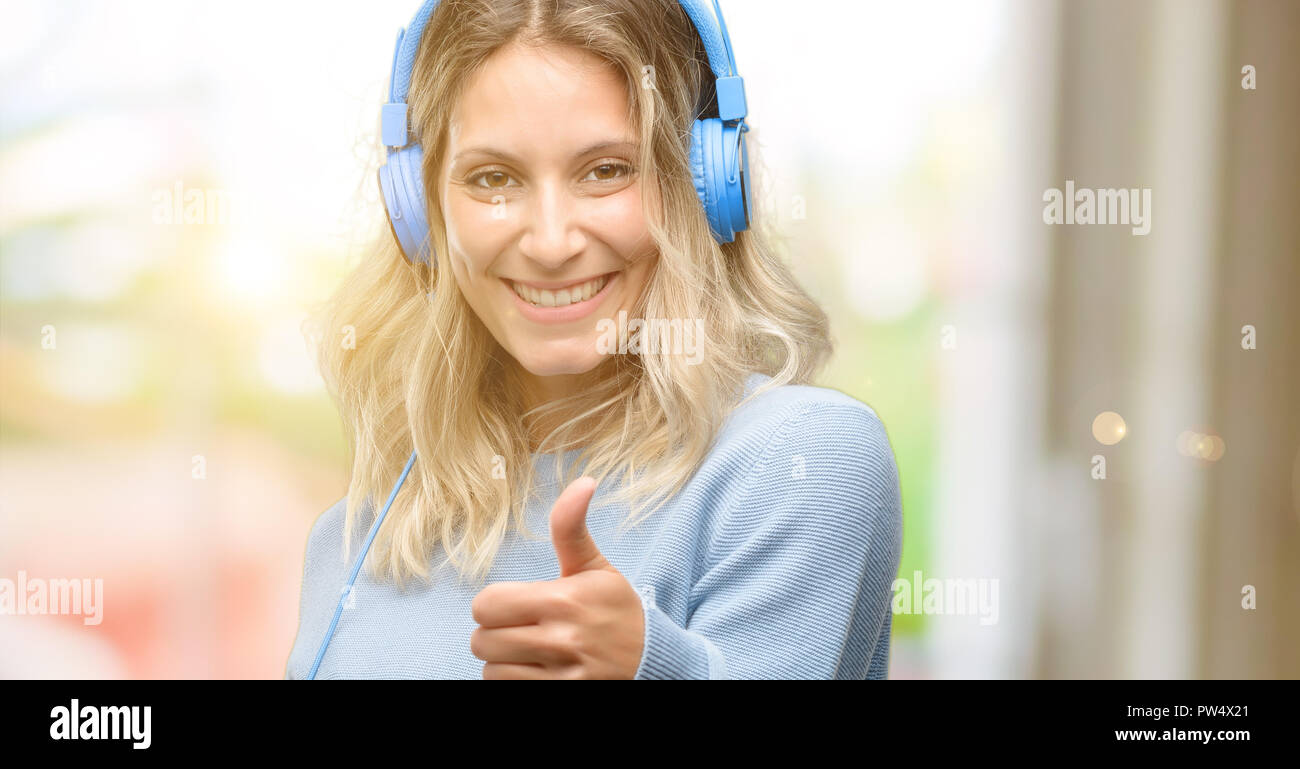 Young beautiful woman listening to music smiling broadly showing thumbs ...