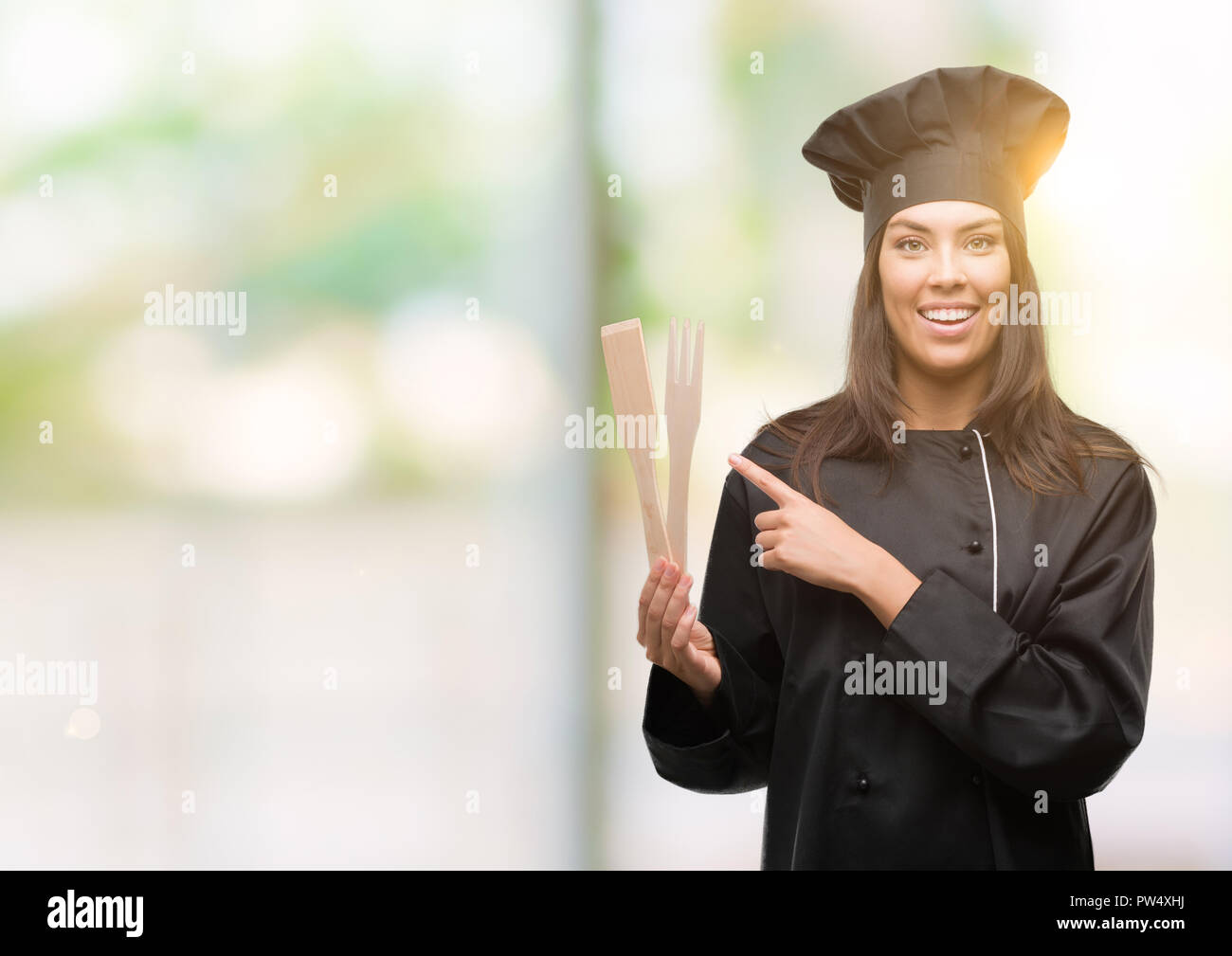 Young hispanic cook woman wearing chef uniform very happy pointing with ...