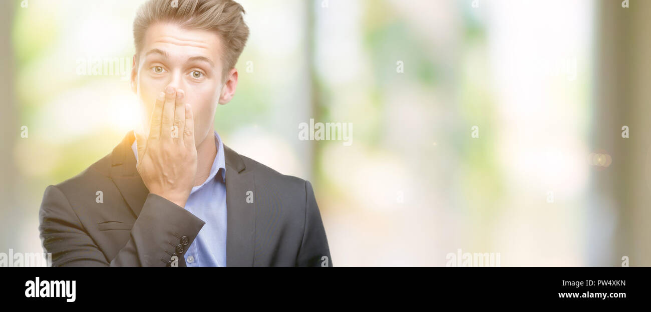 Young handsome blond business man cover mouth with hand shocked with ...