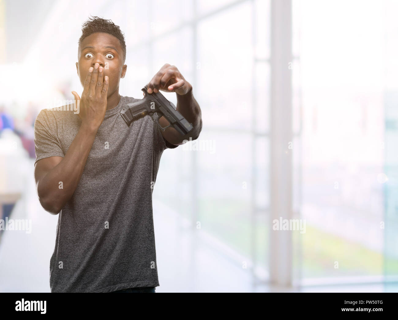Young african american man holding a gun cover mouth with hand shocked ...