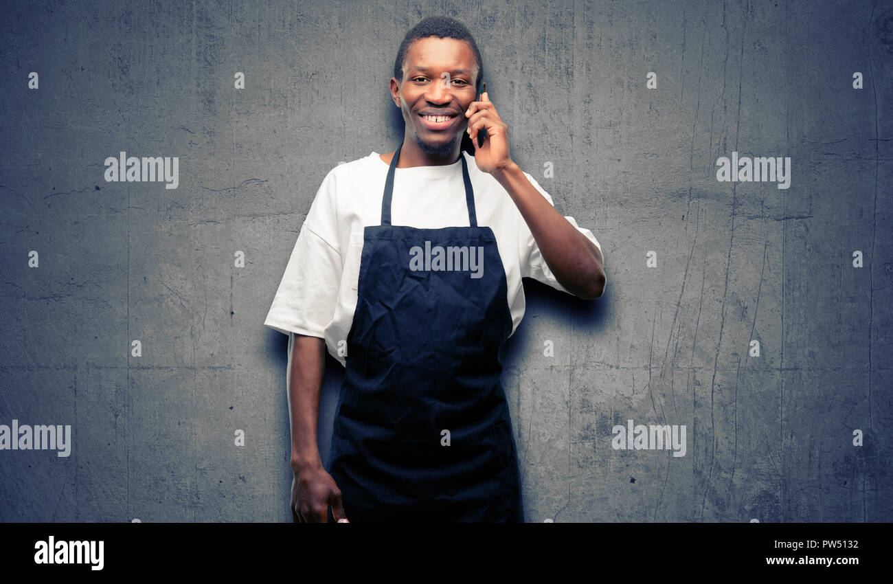 African man shop owner wearing apron happy talking using a smartphone ...