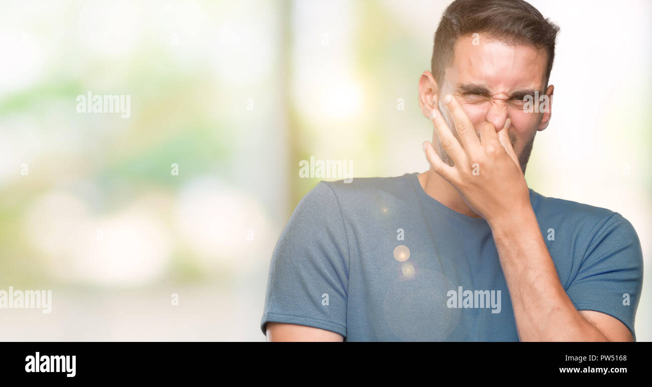 Handsome young casual man smelling something stinky and disgusting ...