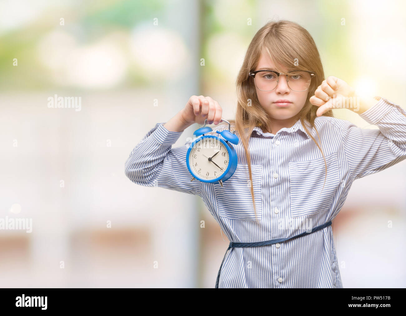 Young blonde child holding alarm clock with angry face, negative sign ...