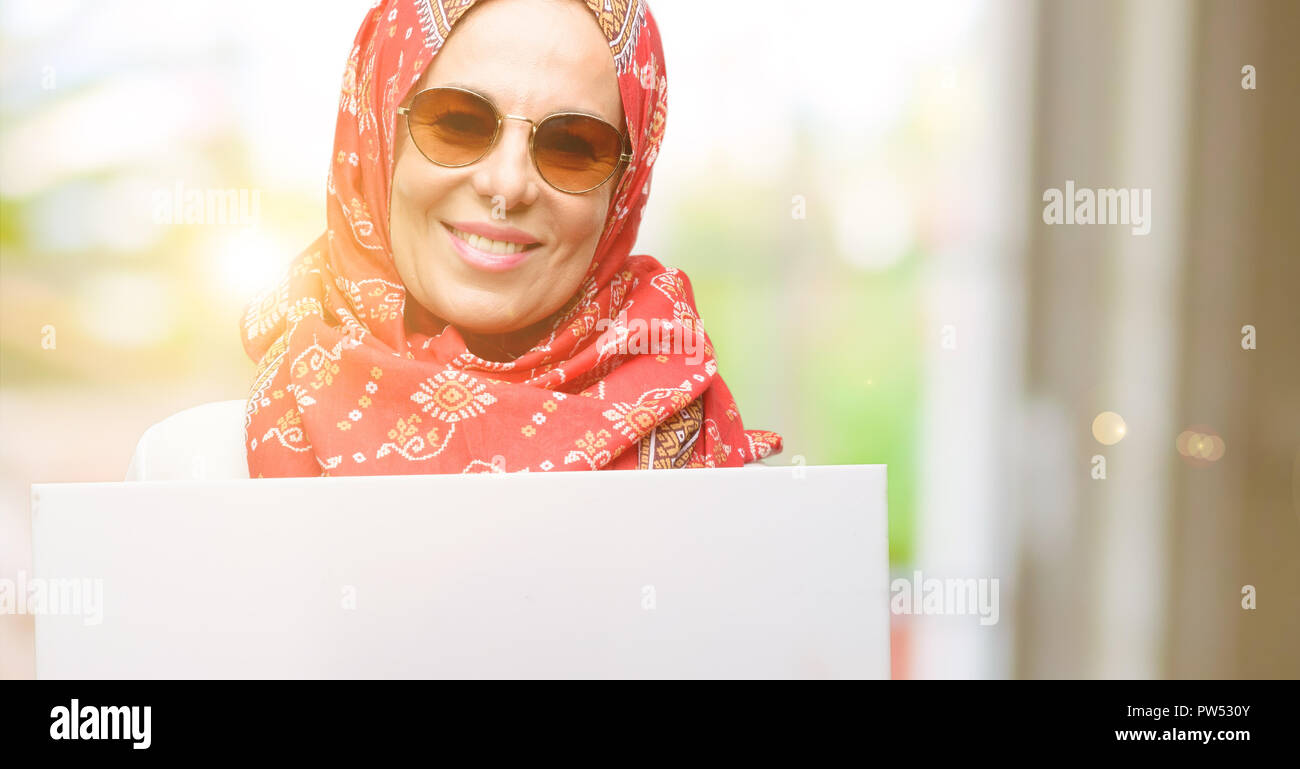 Middle age muslim arab woman wearing hijab holding blank advertising ...