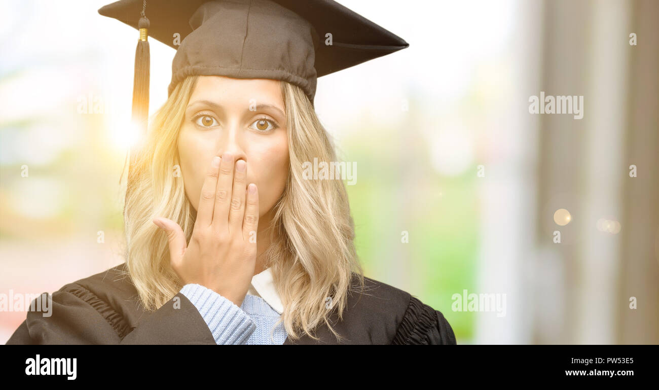 Young graduate woman covers mouth in shock, looks shy, expressing ...