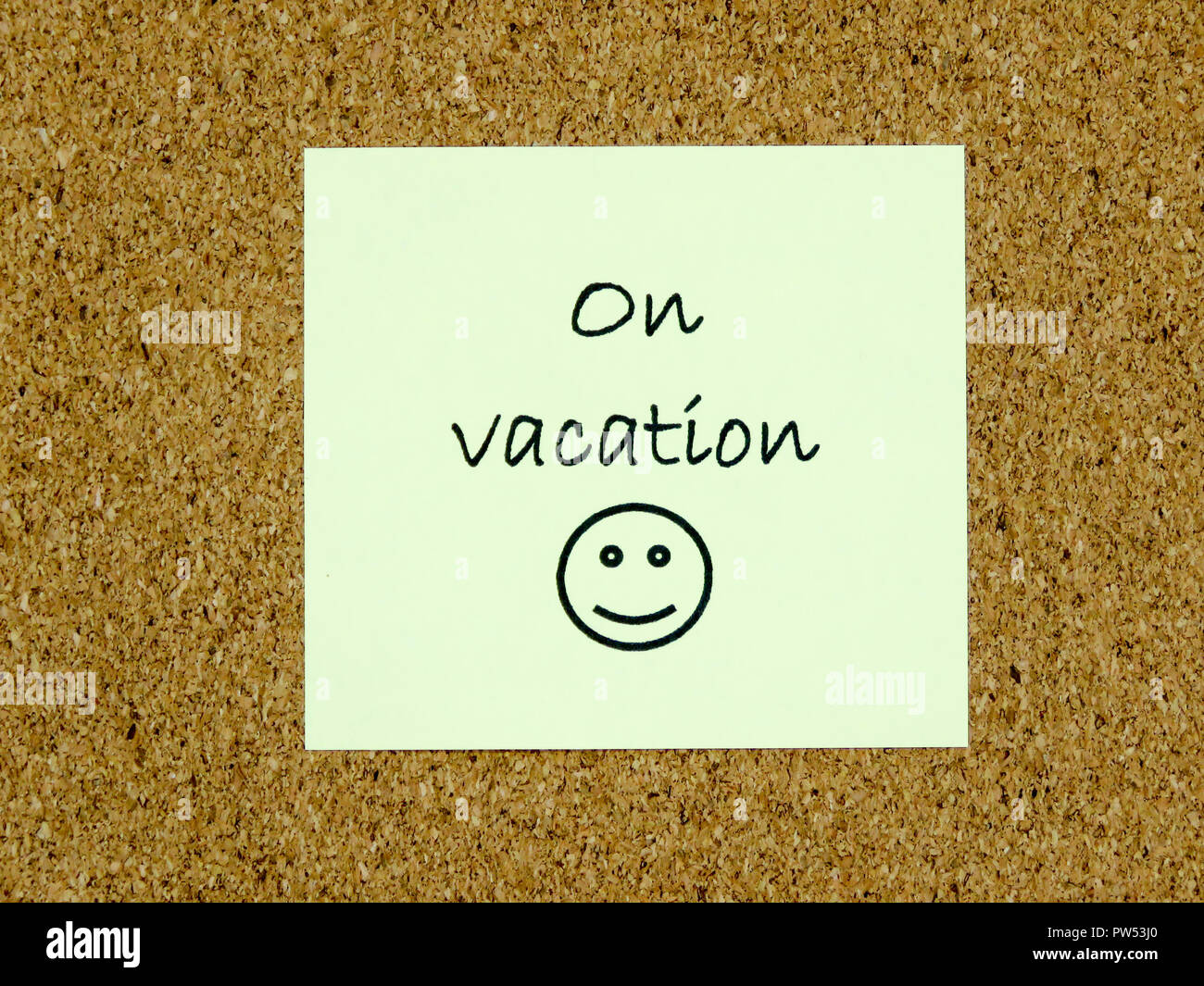 A yellow sticky note with on vacation written on it on a cork board ...