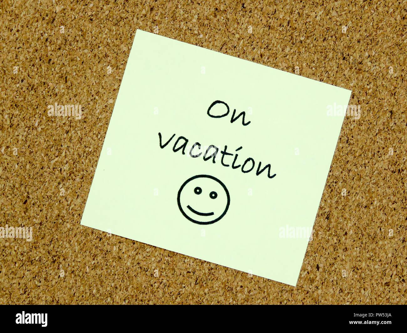 A yellow sticky note with on vacation written on it on a cork board ...