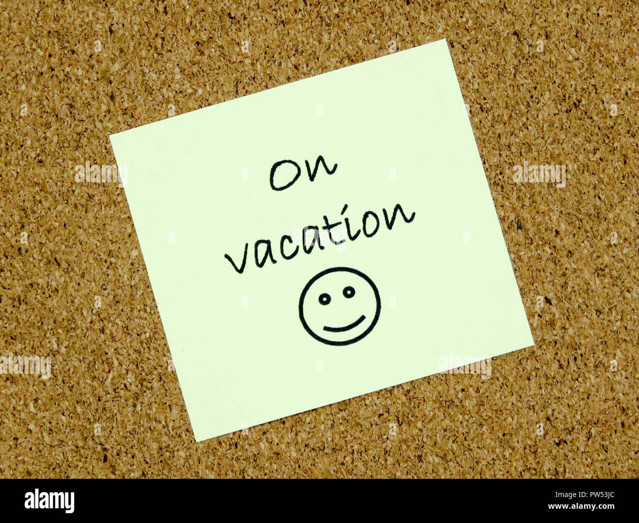 A yellow sticky note with on vacation written on it on a cork board ...