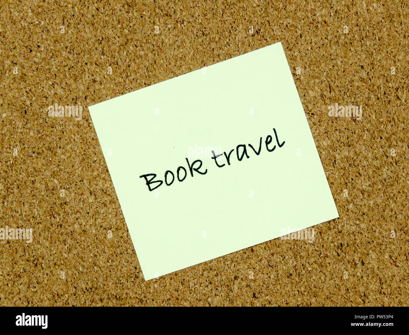 A yellow sticky note with book travel written on it on a cork board ...