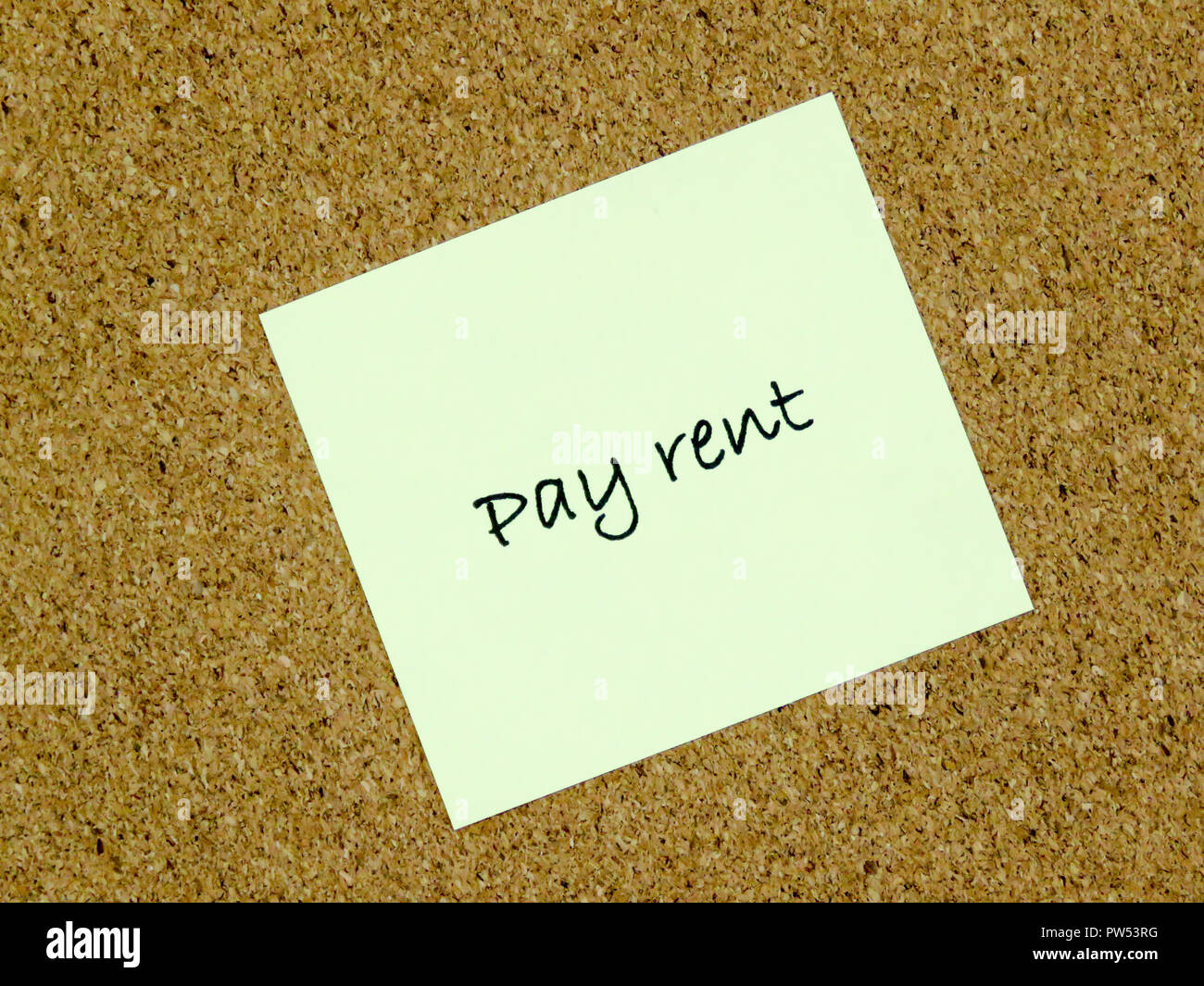 A yellow sticky note with pay rent written on it on a cork board ...