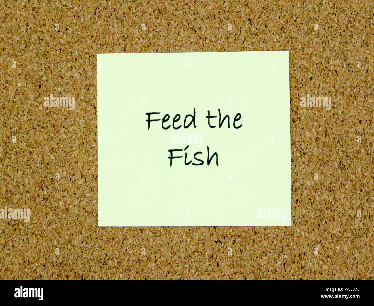 A yellow sticky note with feed the fish written on it on a cork board ...