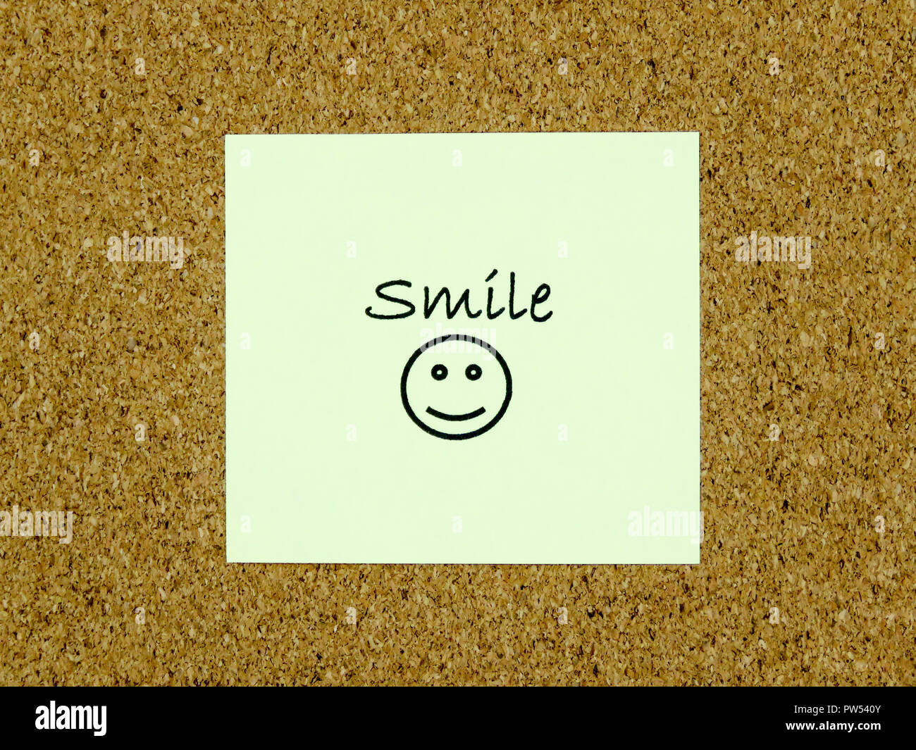 A yellow sticky note with smile written on it on a cork board ...