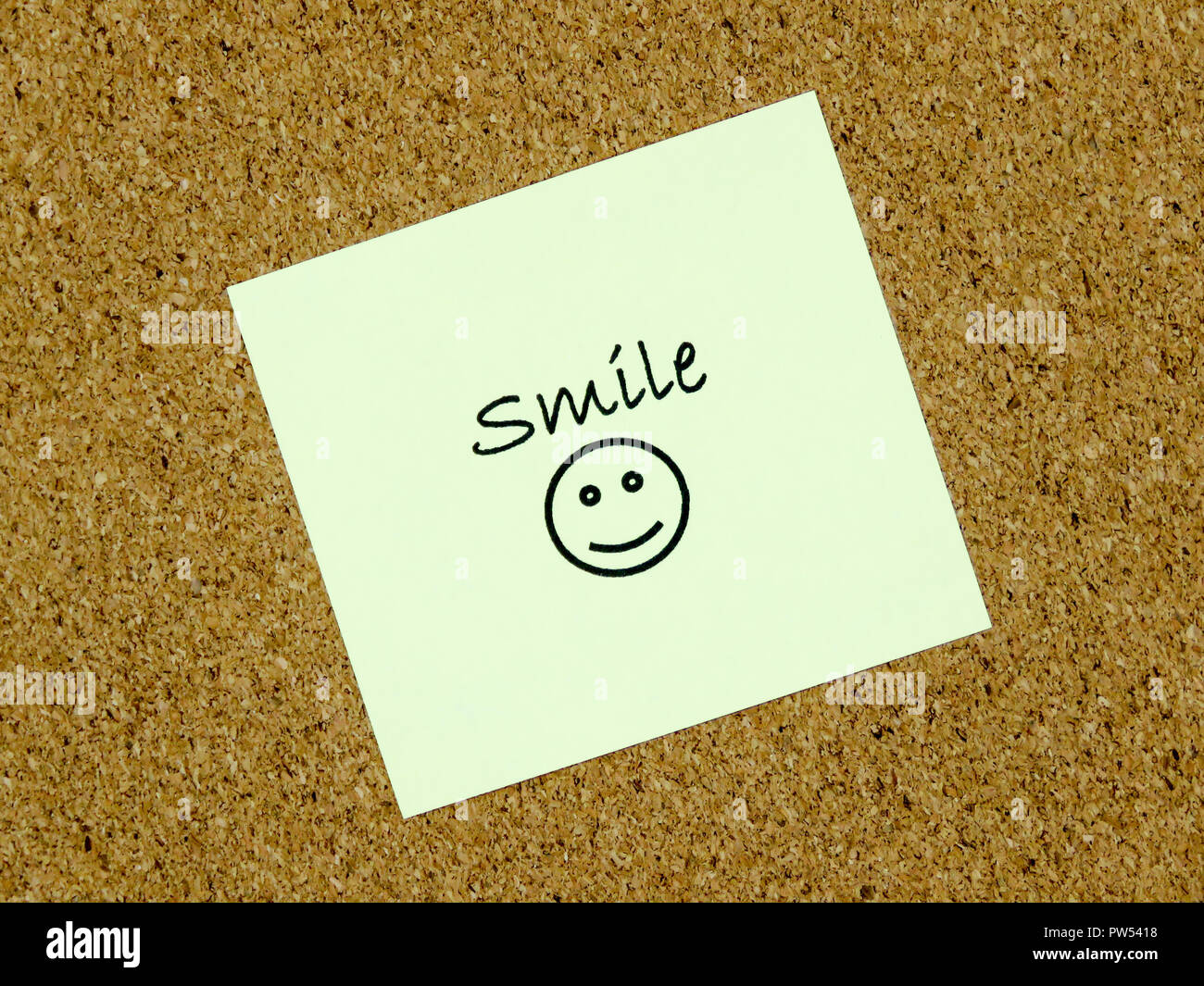 A yellow sticky note with smile written on it on a cork board ...