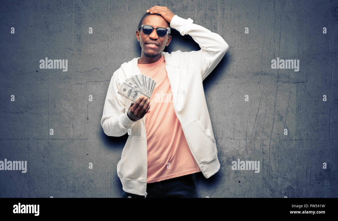 African man holding dollar bank notes terrified and nervous expressing ...