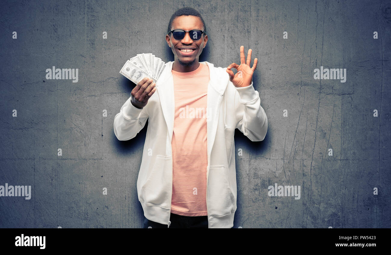 African man holding dollar bank notes doing ok sign gesture with both ...