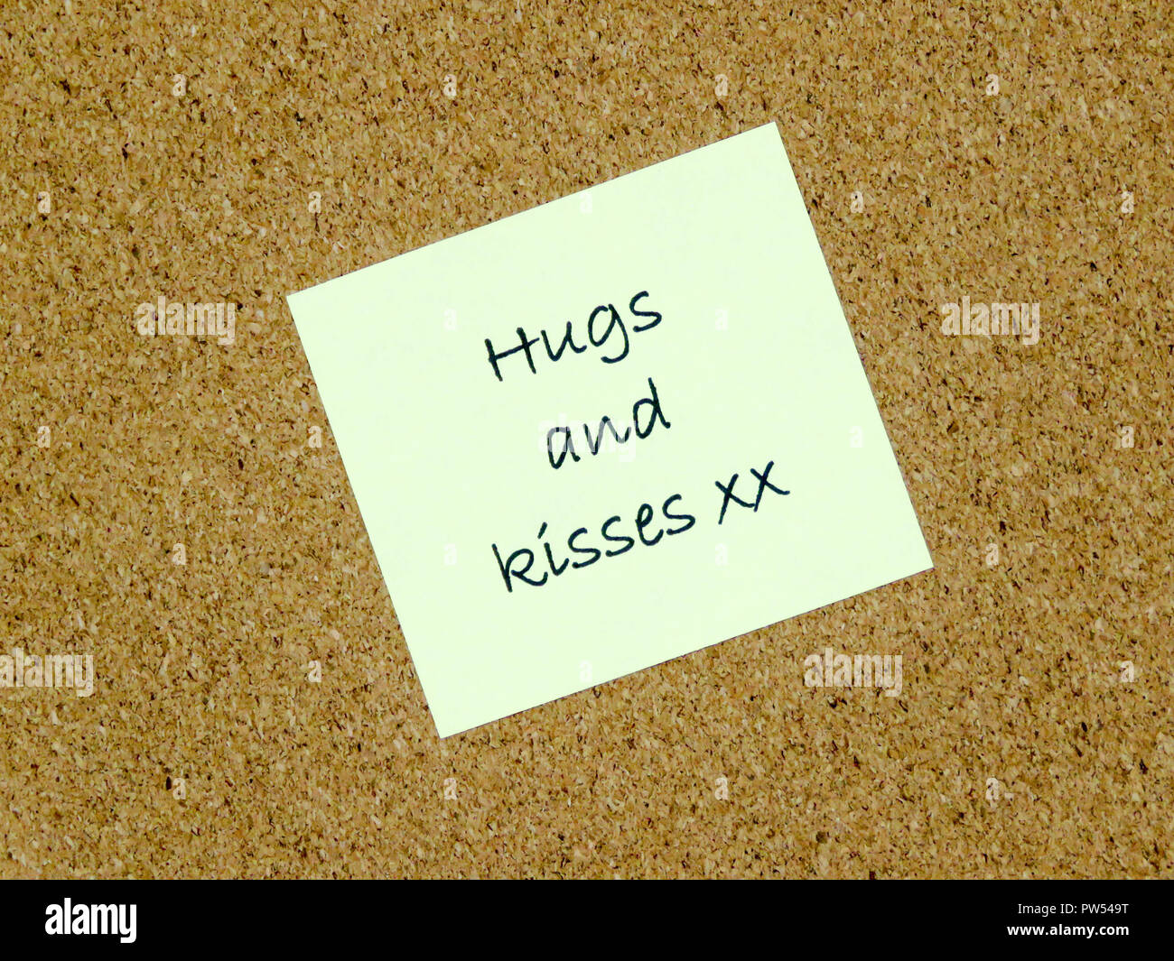 A yellow sticky note with hugs and kisses written on it on a cork board ...