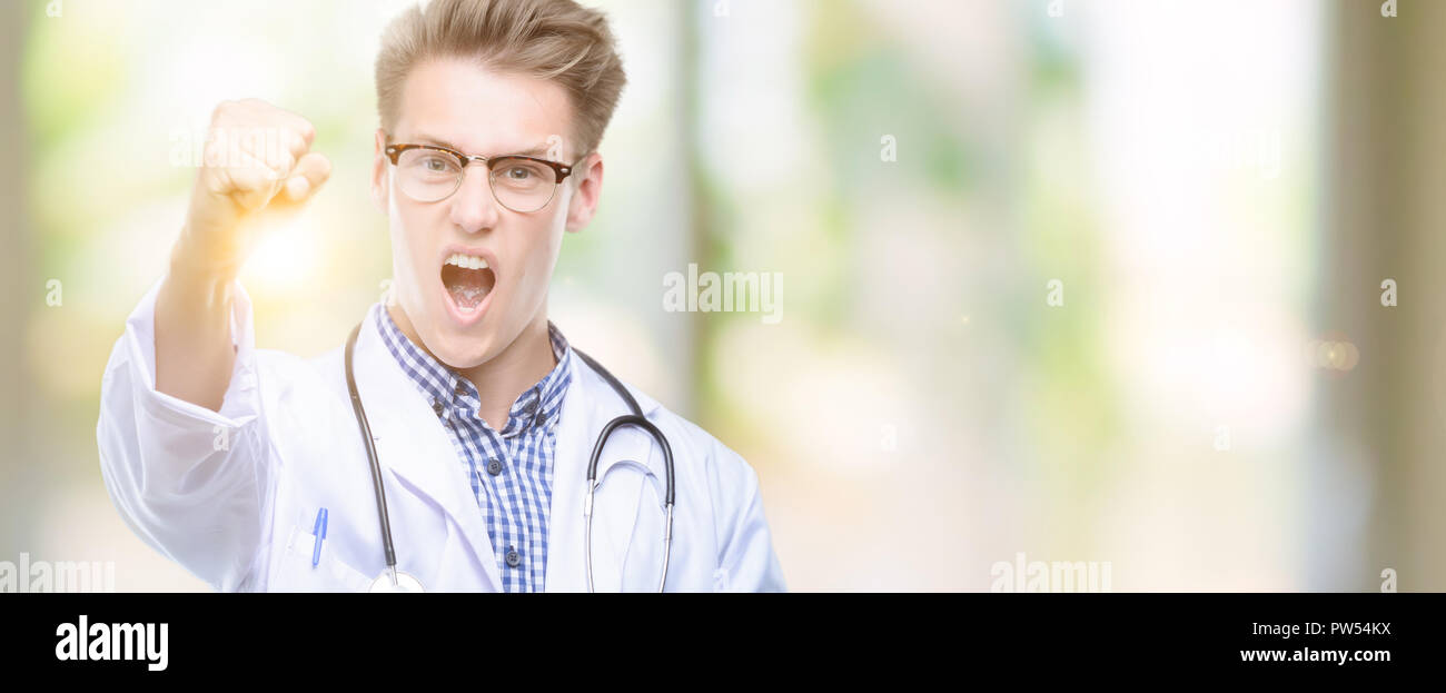 Young handsome blond doctor annoyed and frustrated shouting with anger ...