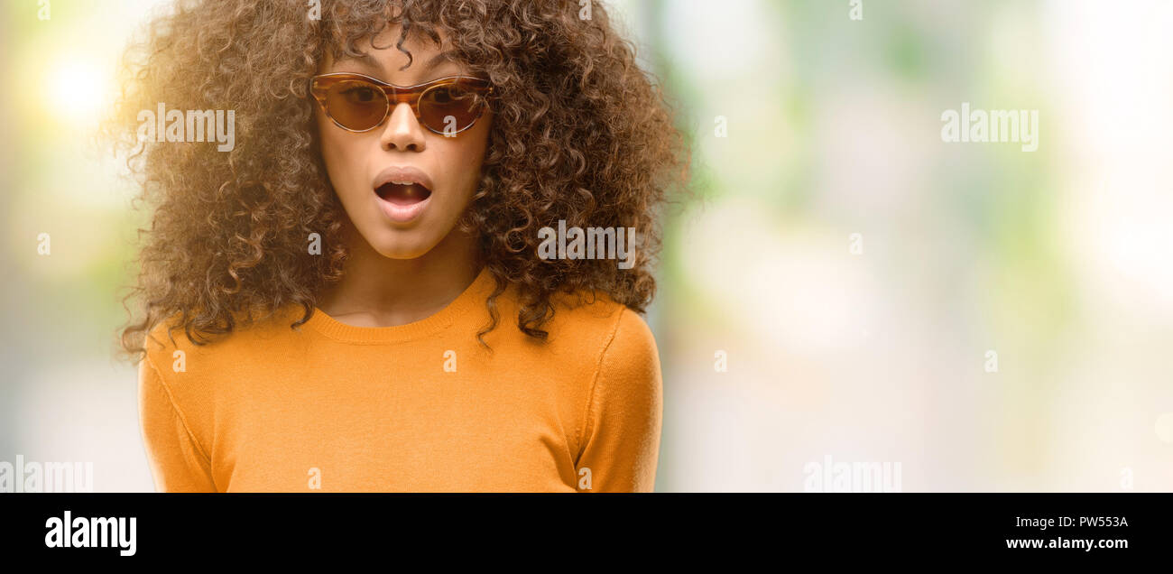 African american woman wearing an orage sweater scared in shock with a ...