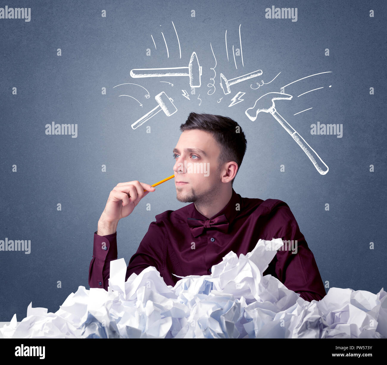 Young businessman sitting behind crumpled paper with drawn hammers ...