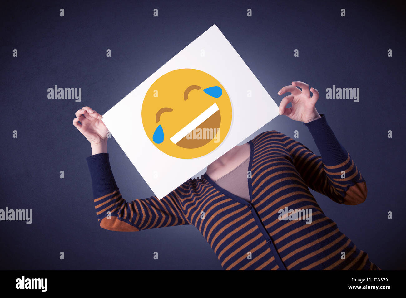 Young casual woman hiding behind a laughing emoticon on cardboard Stock ...