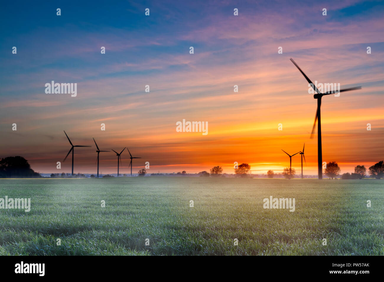 Wind turbines in foggy field with dramatic colorful sunset sky ...