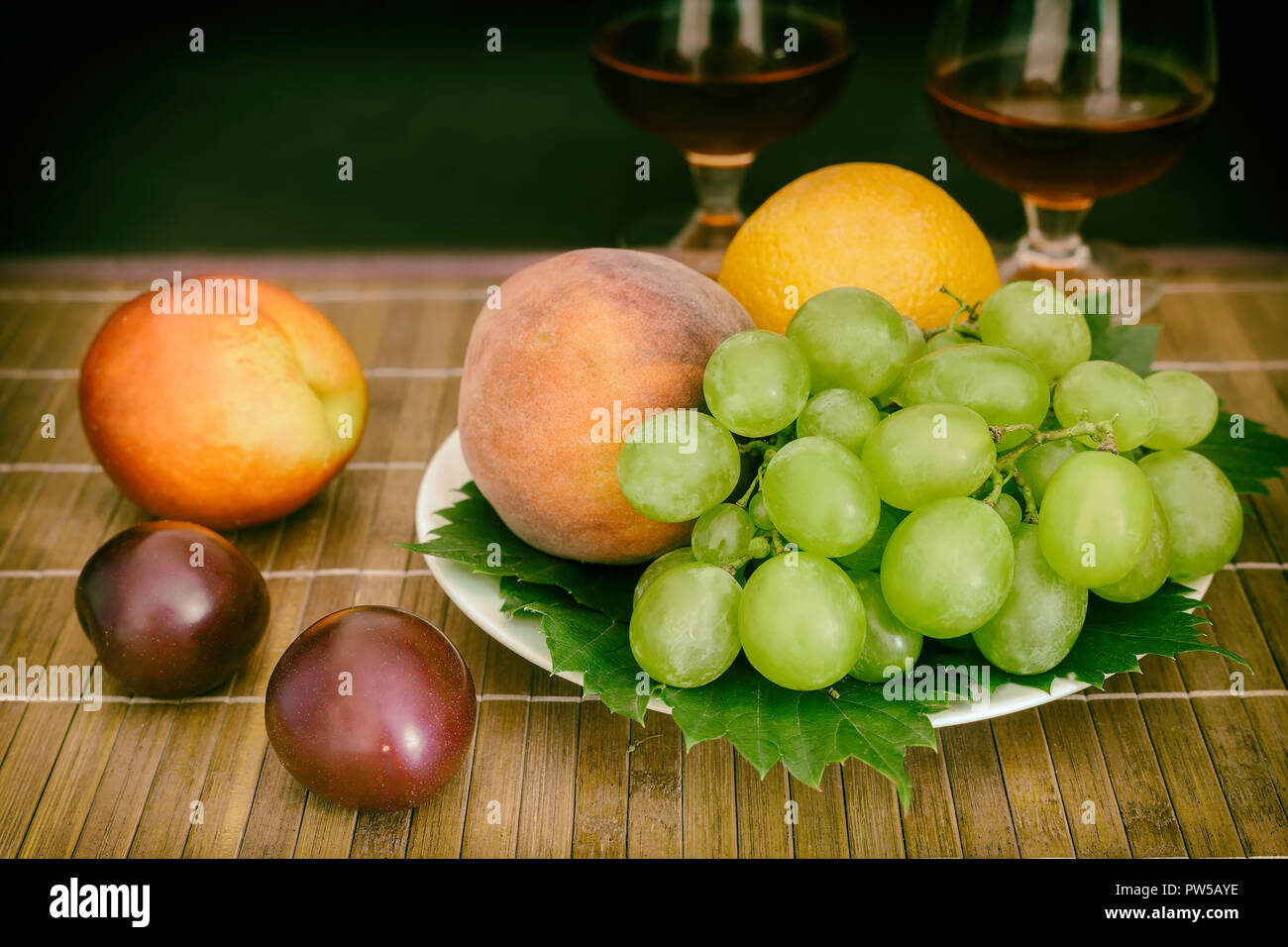 Still life: on the table on a plate are fruits, next to two glasses of ...