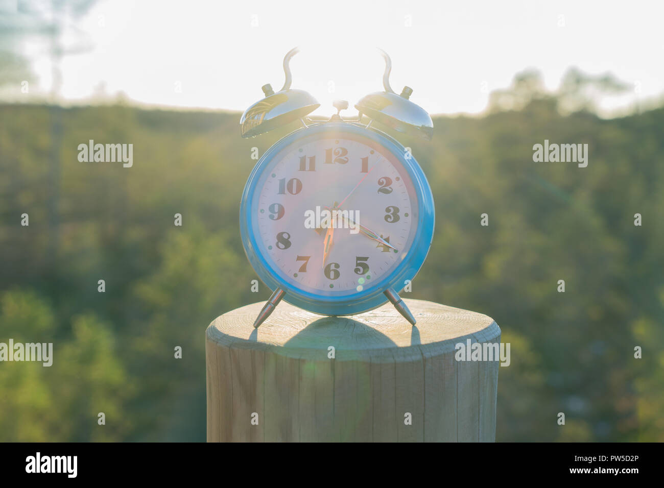 Vintage blue alarm clock on summer forest background. Daylight saving ...