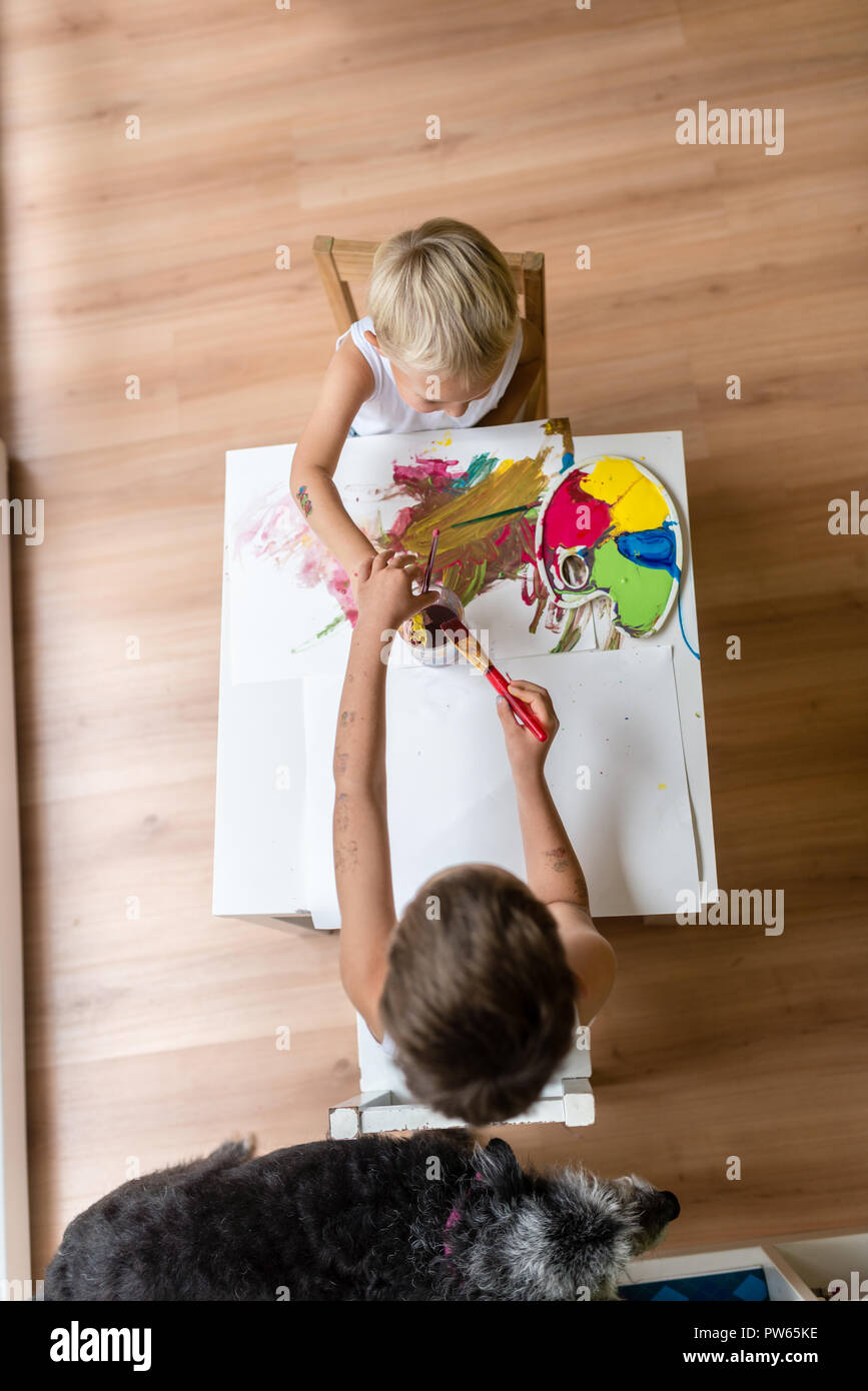 Aerial view of children painting with watercolors dipping a brush into ...