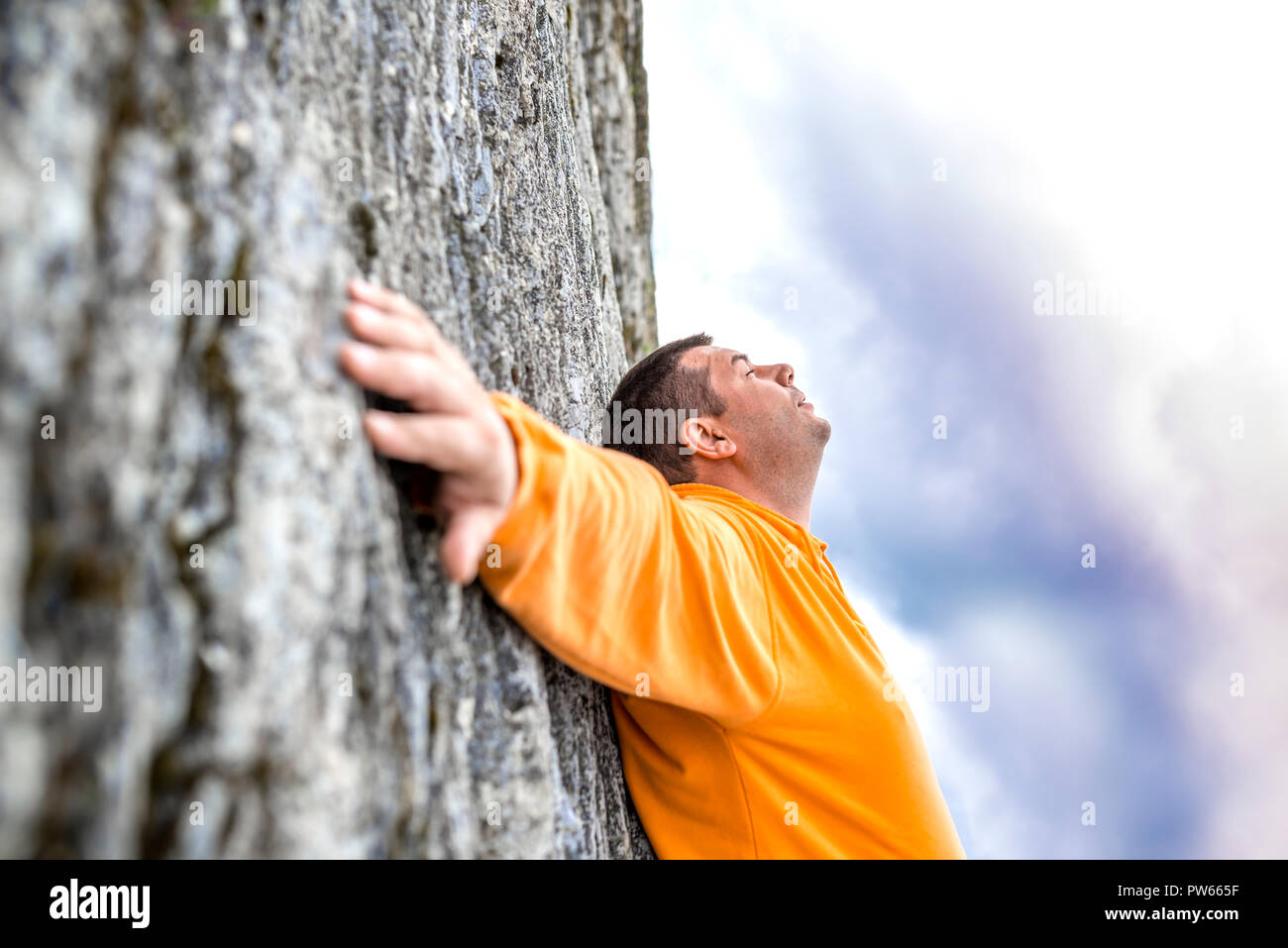 Young man leaning on rock of steep mountain climb with hands wide open ...