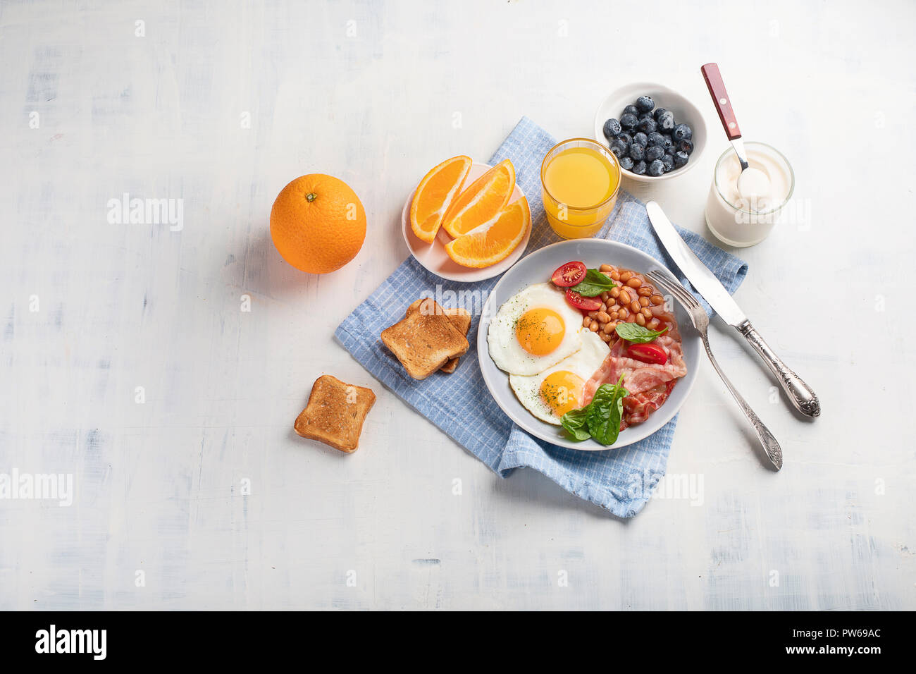 Plate of breakfast with fried eggs, bacon, beans, orange juice and ...