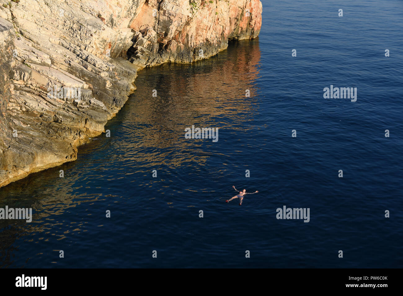 Human floating in the beautiful deep blue sea next to the rocky cliff ...