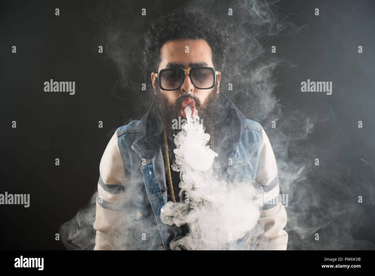 Vaping man holding a mod. A cloud of vapor. Black background. Vaping an ...