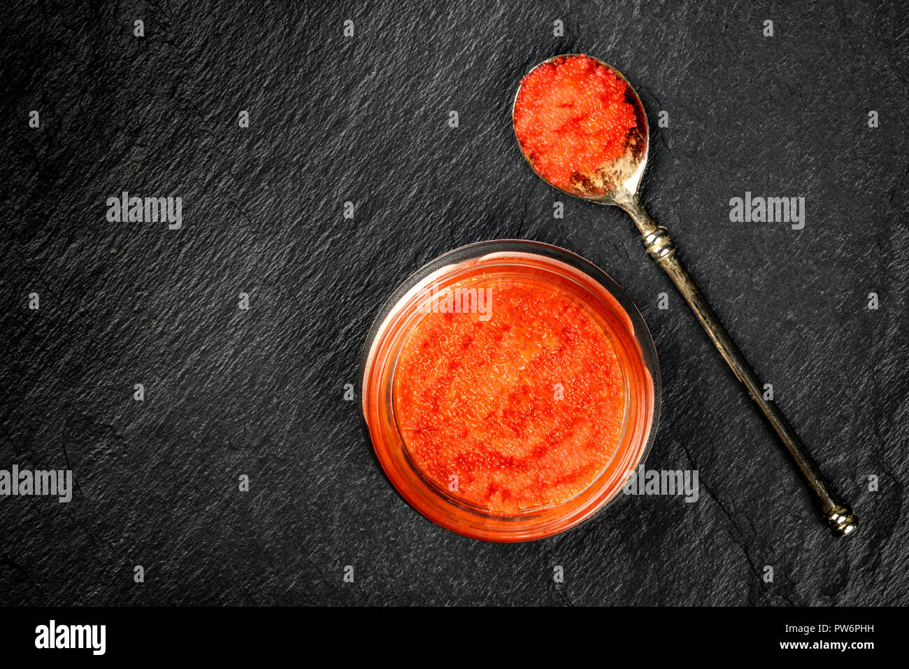Red fish roe in a jar and in a spoon, shot from above on a black ...