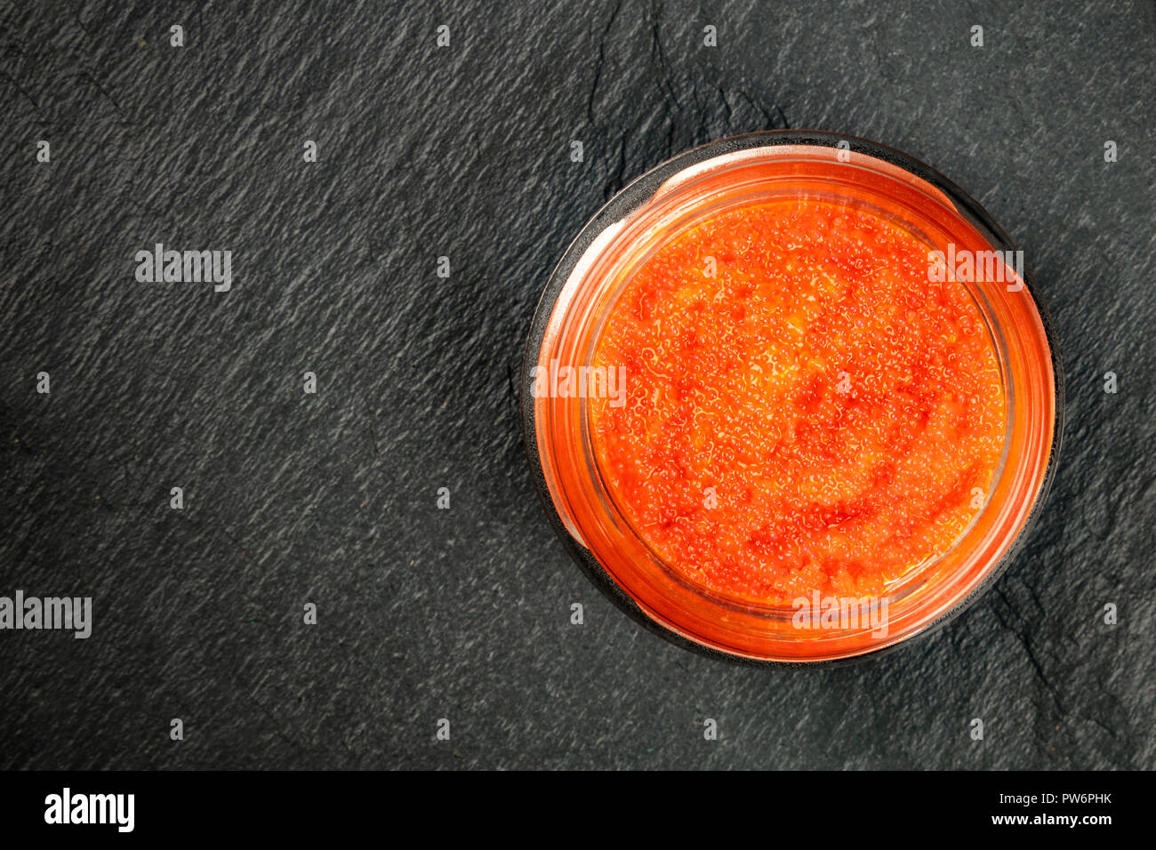 Red fish roe in a jar, shot from above on a black background with copy ...
