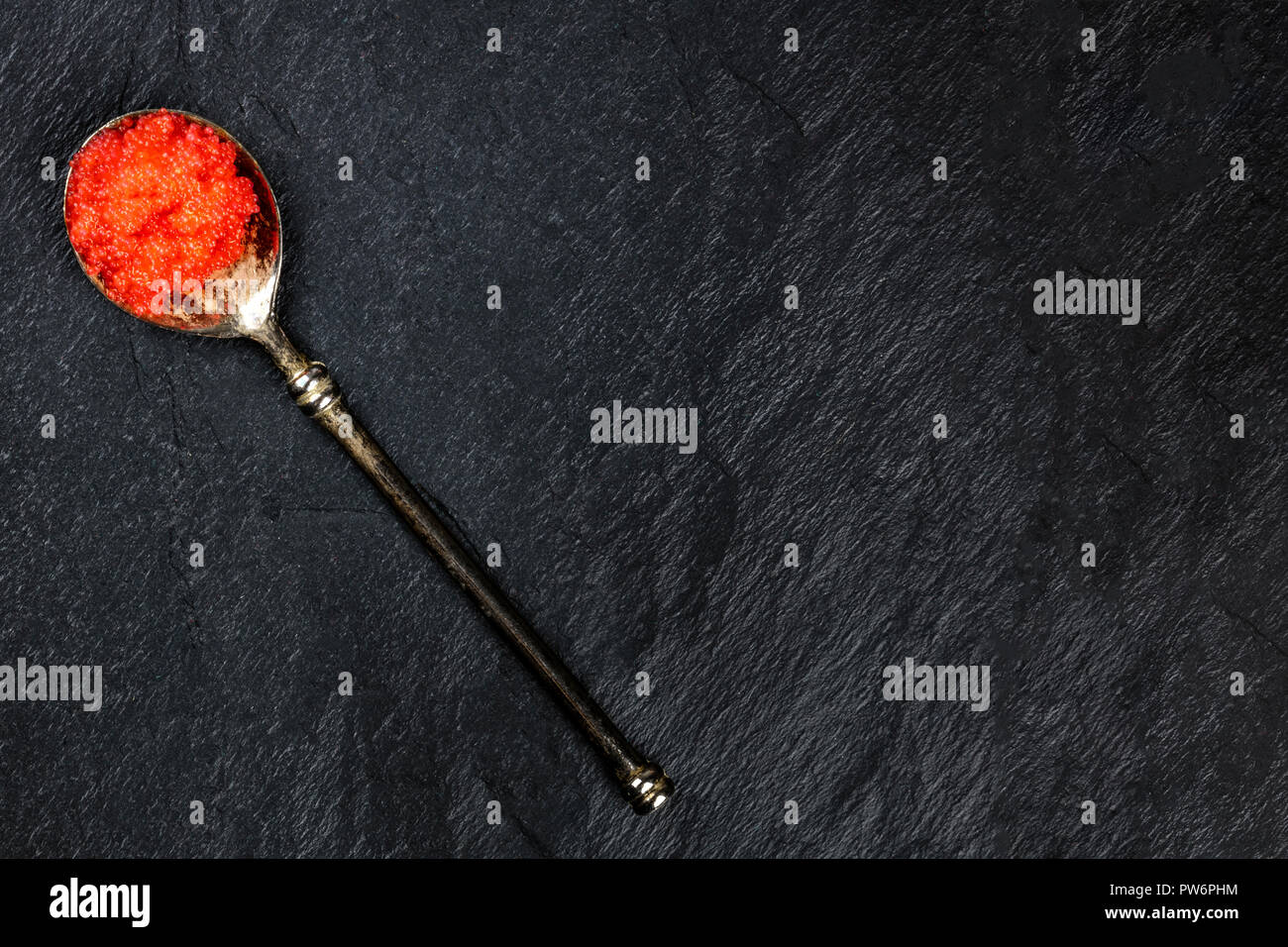 Red fish roe in a spoon, shot from above on a black background with ...
