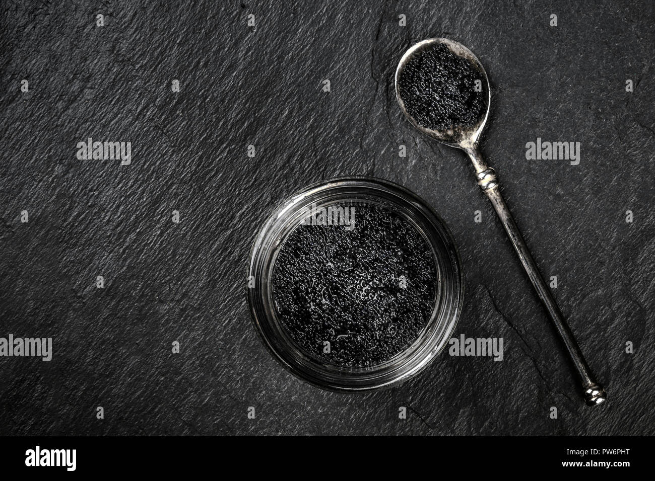 Black fish roe in a jar and in a spoon, shot from the top on a black ...