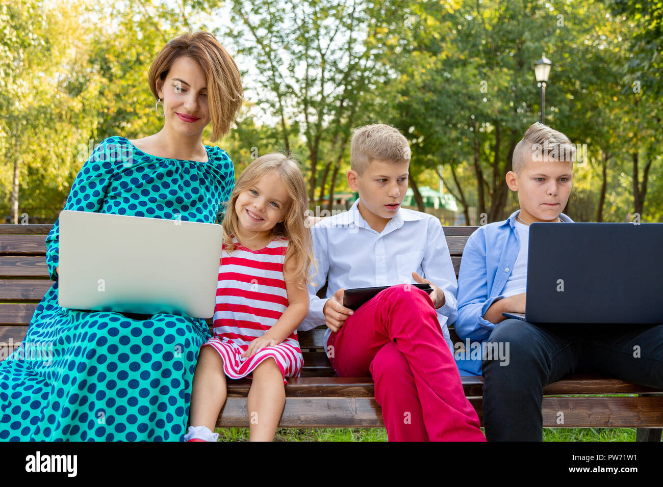 Young family with gadgets sitting on the bench Stock Photo - Alamy