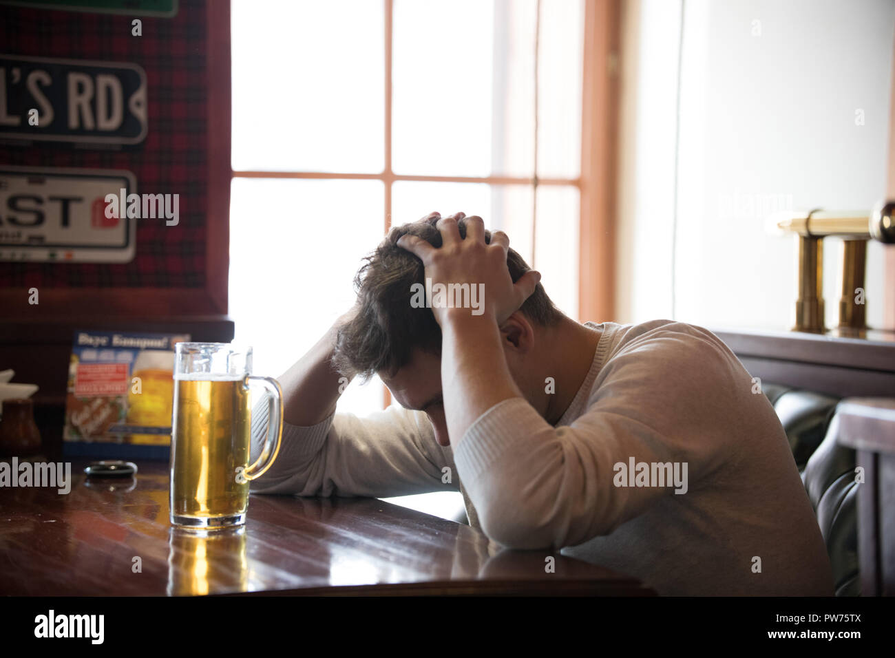 Stressed young man drinks beer in the pub. The man holds his head Stock ...