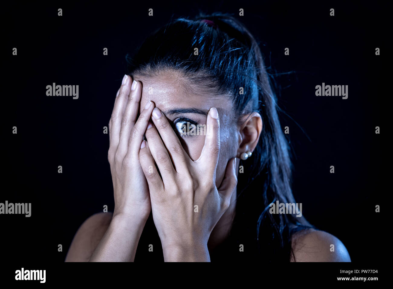 Close up portrait terrified young attractive latin woman looking frightened through her fingers ...