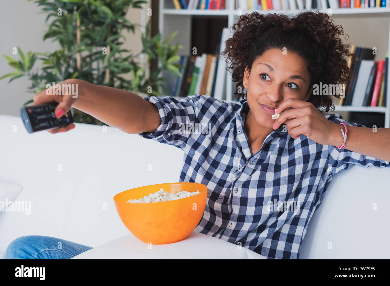 Afro woman sitting at home with remote control watching tv Stock Photo ...