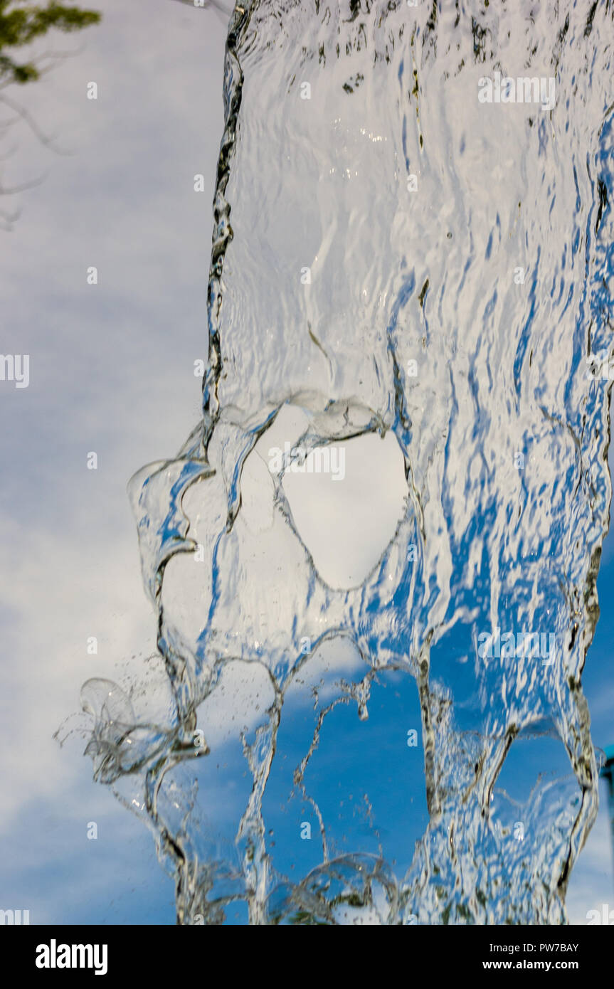 transparent falling water vertical flows against a blue sky and green ...