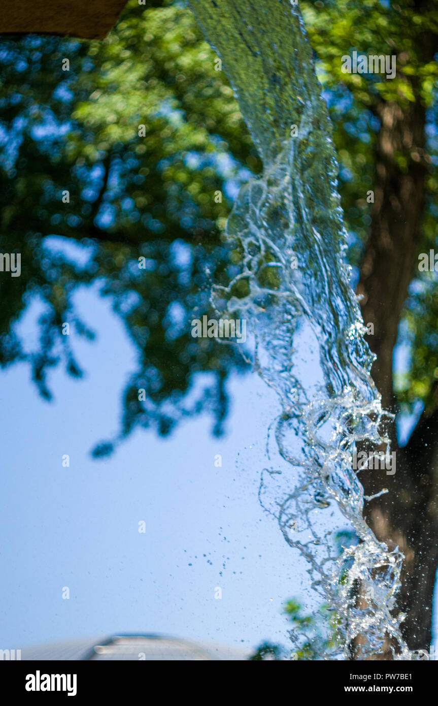 transparent falling water vertical flows against a blue sky and green ...