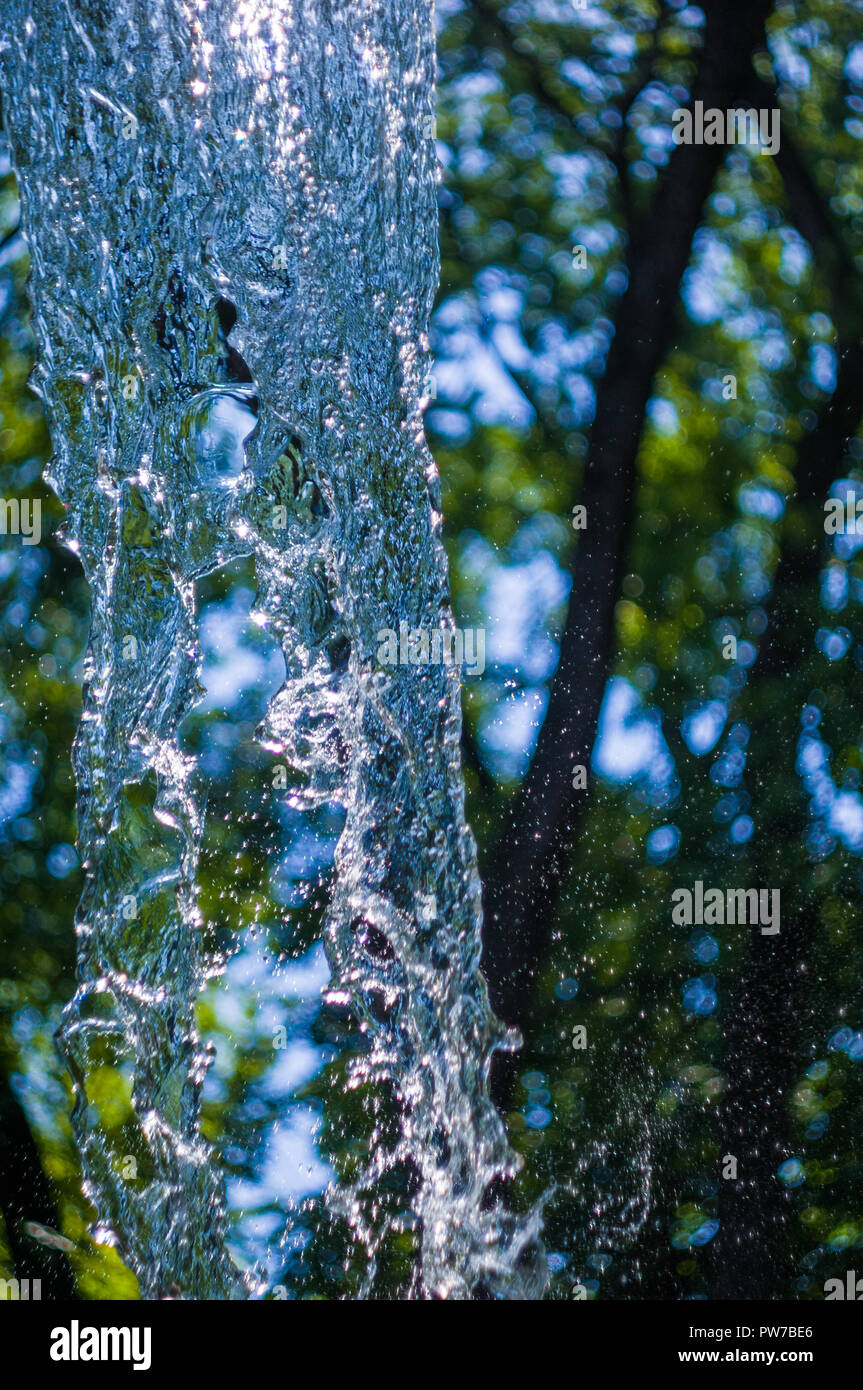 transparent falling water vertical flows against a blue sky and green ...