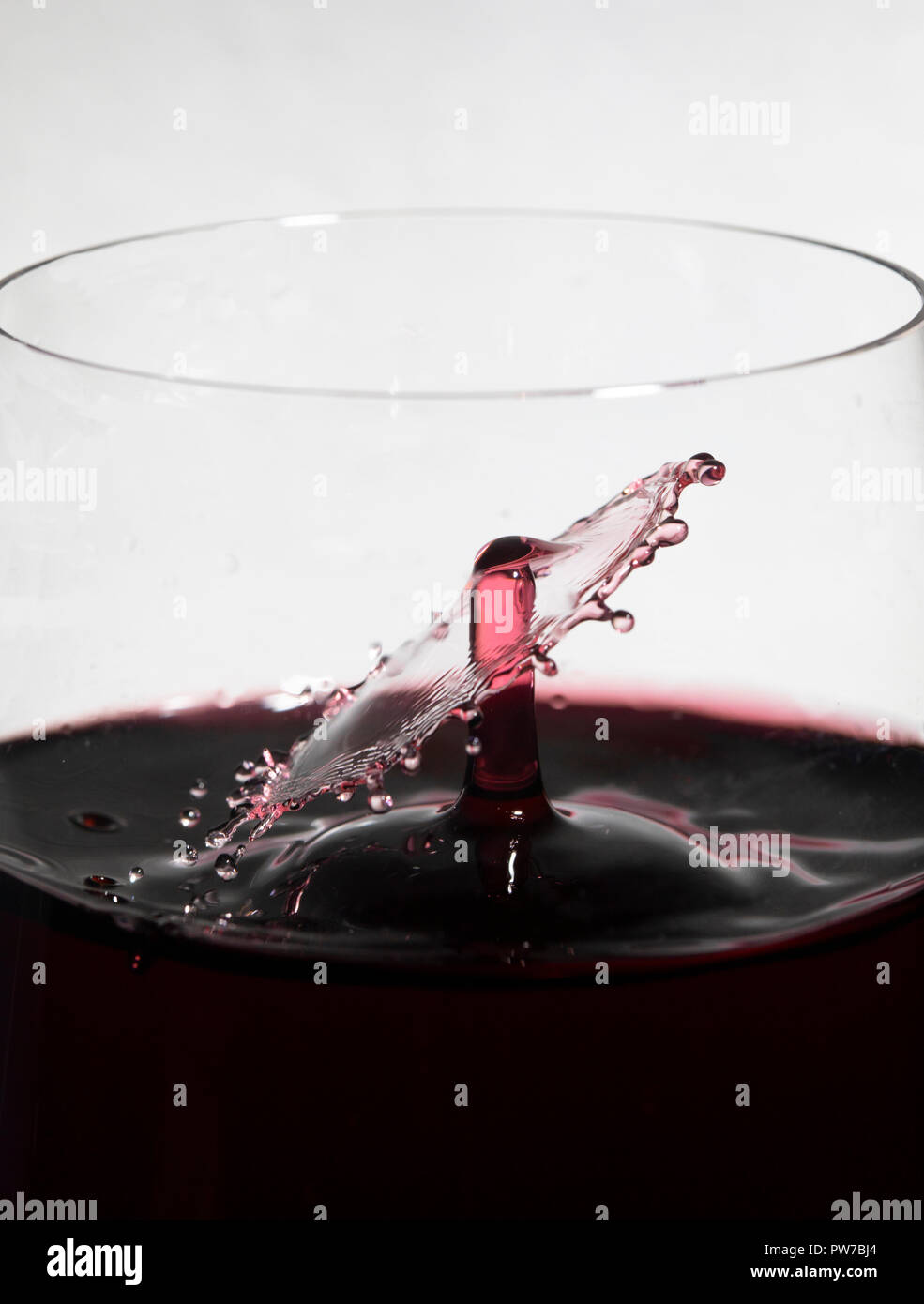 Falling wine drop collides with wine splashing in glass, creating a ...