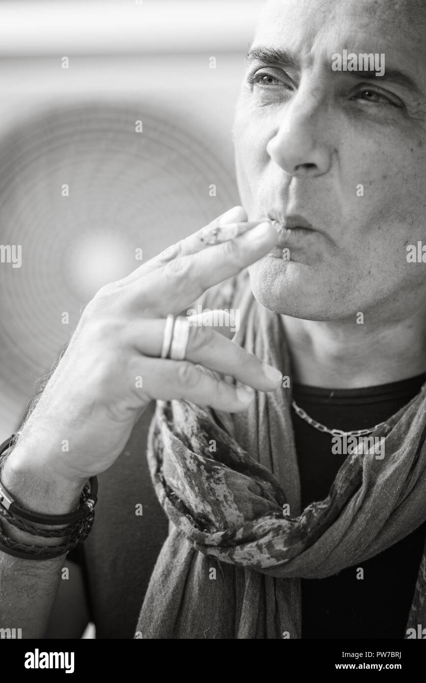 A 50y man is smoking a cigarette. Black and white. The fan coil of an ...