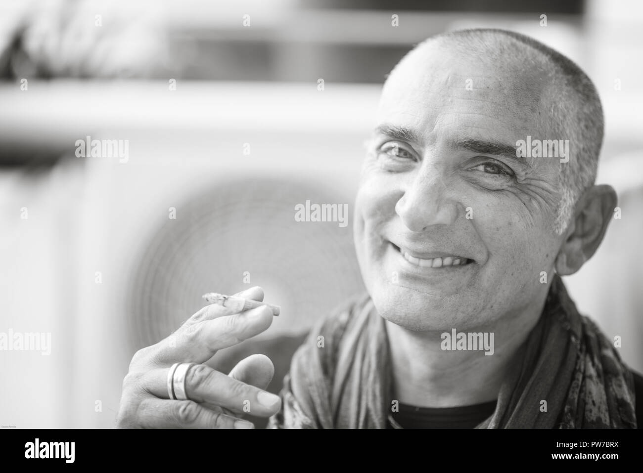 A 50y man is smoking a cigarette. Black and white. The fan coil of an ...