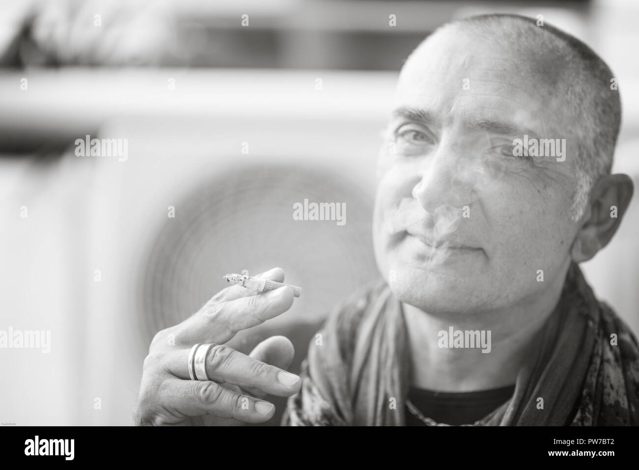 A 50y man is smoking a cigarette. Black and white. The fan coil of an ...