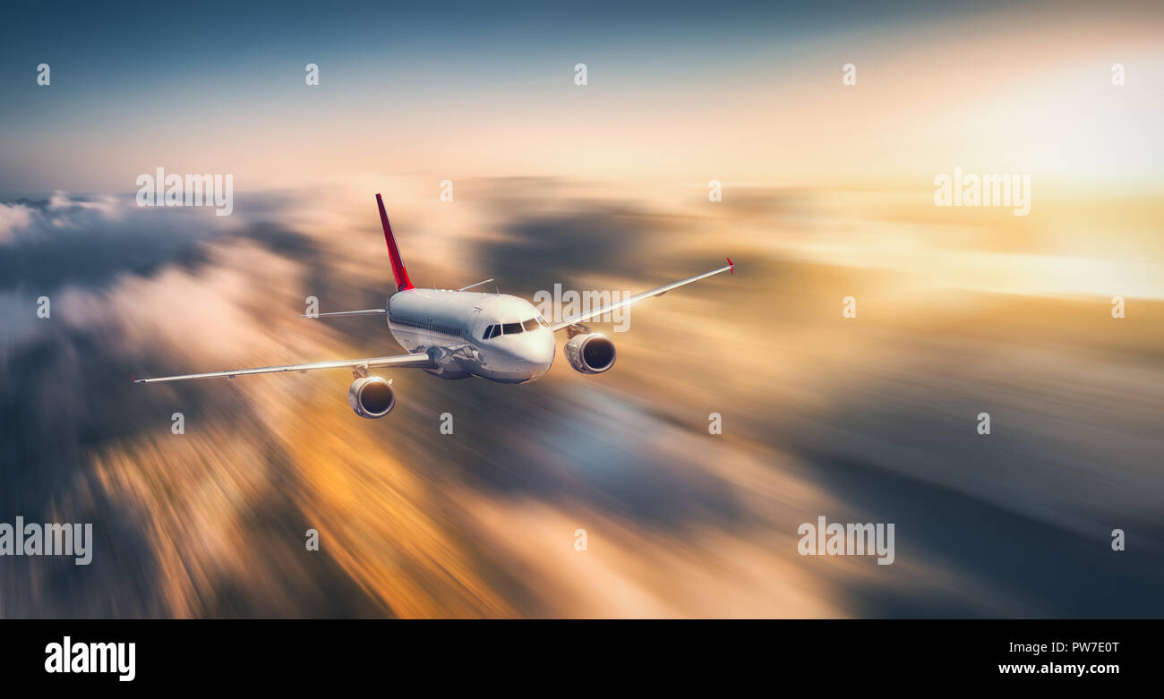 White airplane is flying in low clouds at sunset. Landscape with ...