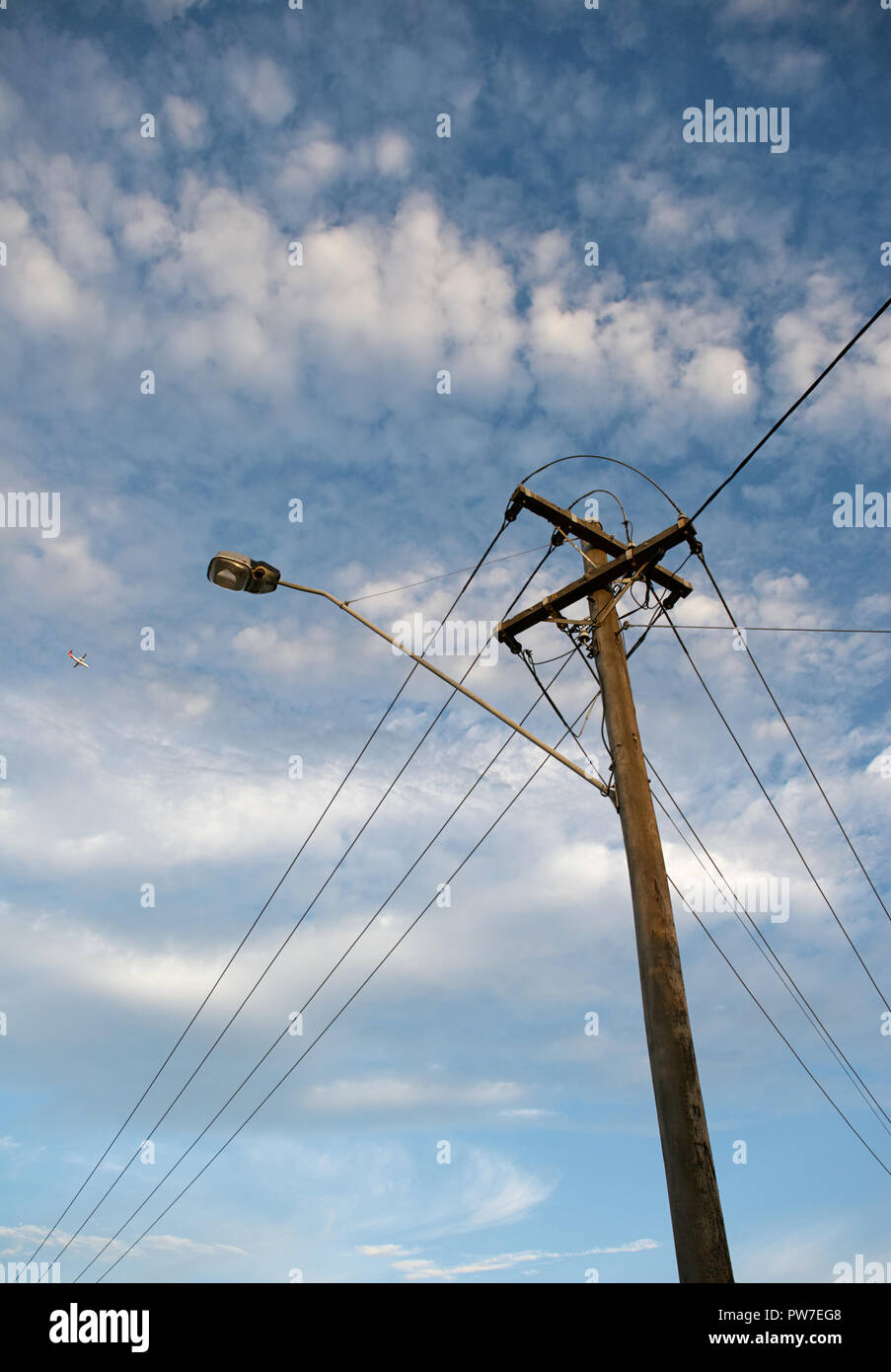 Street light, power lines against a dramatic blue sky and airplane high ...